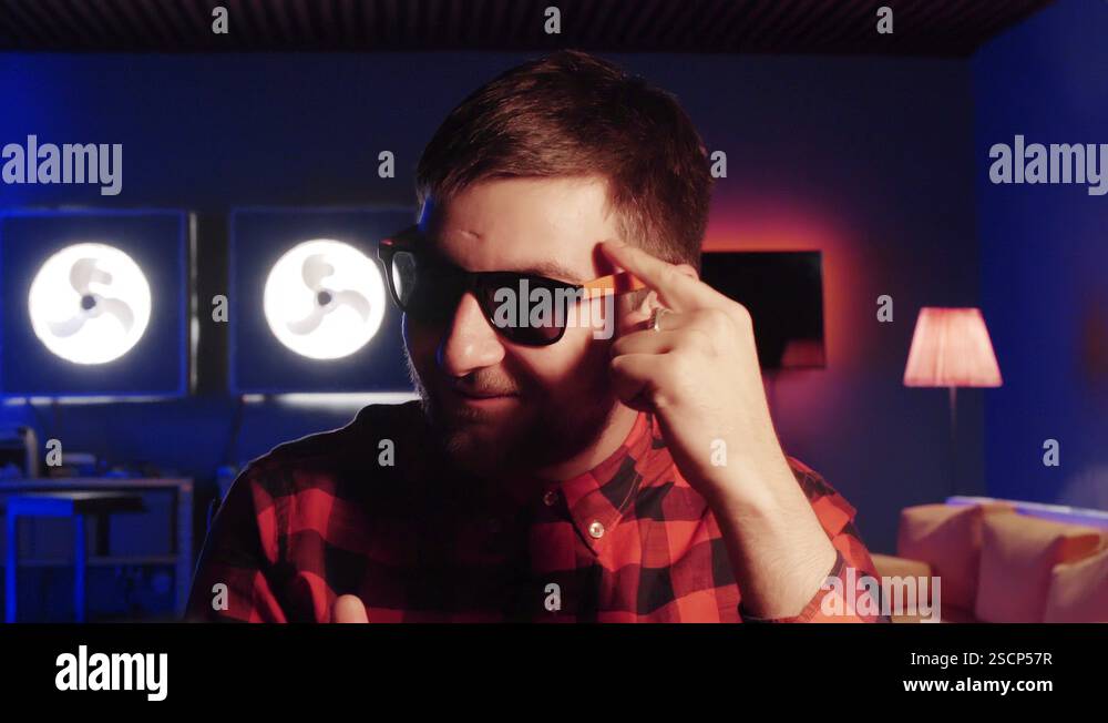 Smiling guy with sunglasses looks at camera and points at his head with ...