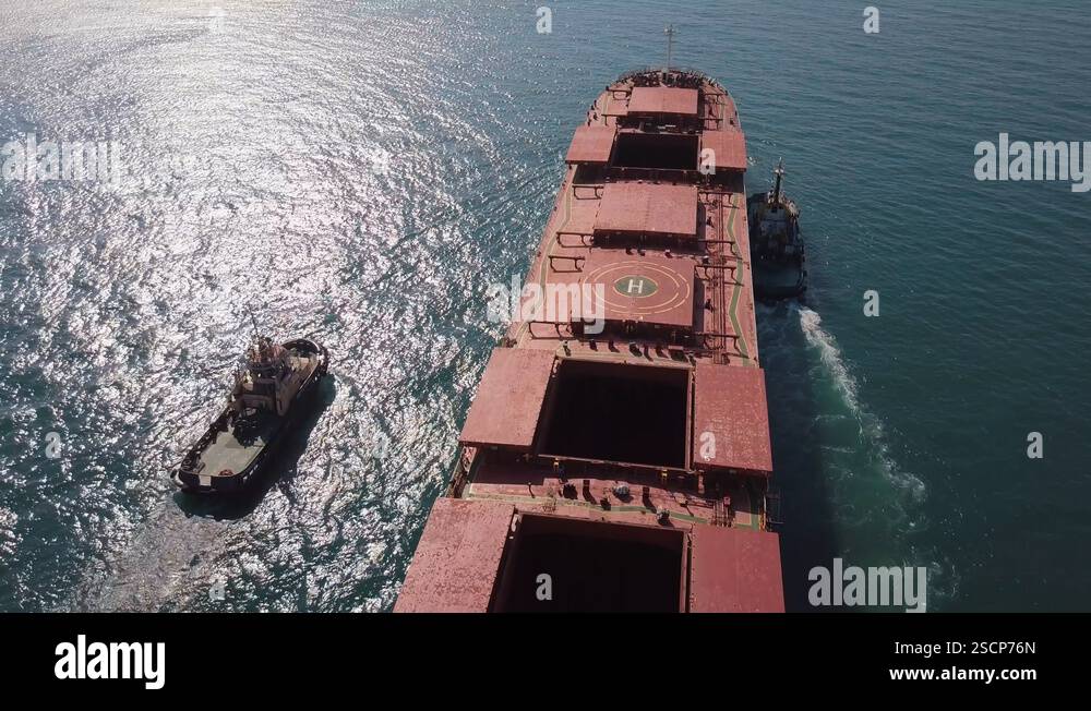 Aerial flight over bulk freighter cruising in open sea with tugs ...