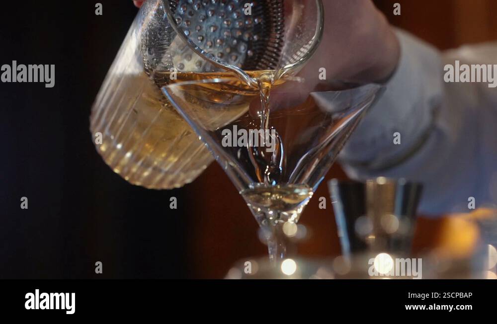 The bartender pours the finished cocktail into a Martini glass, close ...