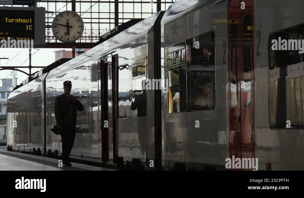 Conductor in uniform entering modern metallic train at Antwerp platform ...