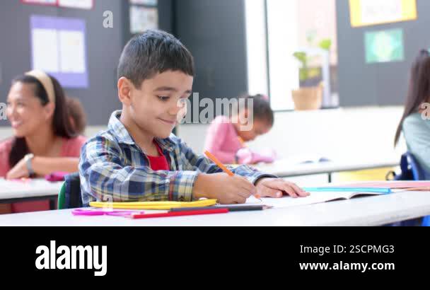 In school, boy writing in notebook with pencil, focusing on classroom ...