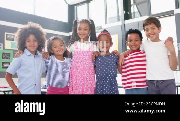 Smiling school children standing together in classroom, arms around ...