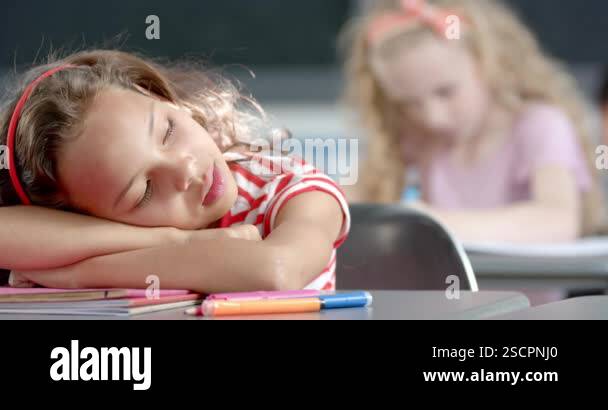 In school, girl sleeping on desk with colorful pens while classmate ...