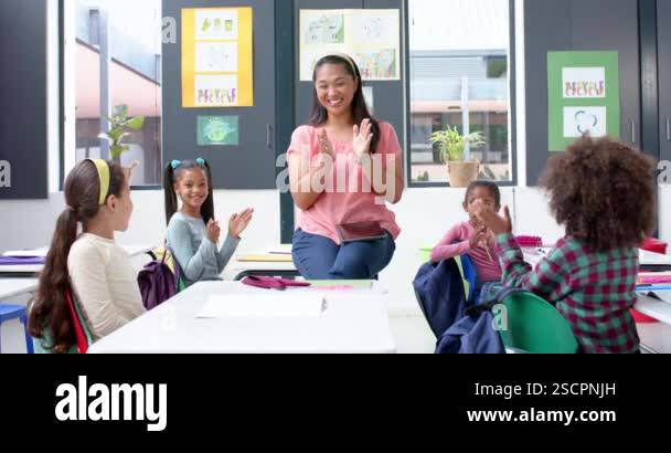 In school, teacher clapping with students in classroom, engaging in ...