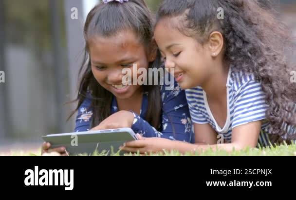 In school, two girls lying on grass using tablet, smiling and engaged. Education, friendship ...