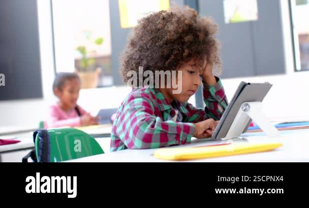 In school, focused boy using tablet for learning in classroom setting. Education, technology ...