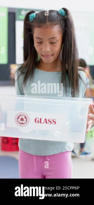 Vertical video: In school, girl holding recycling bin labeled glass and ...