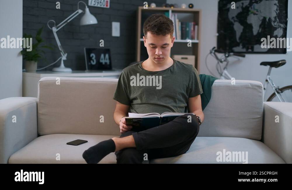 A boy is attentively reading a book on a couch when he gets distracted ...