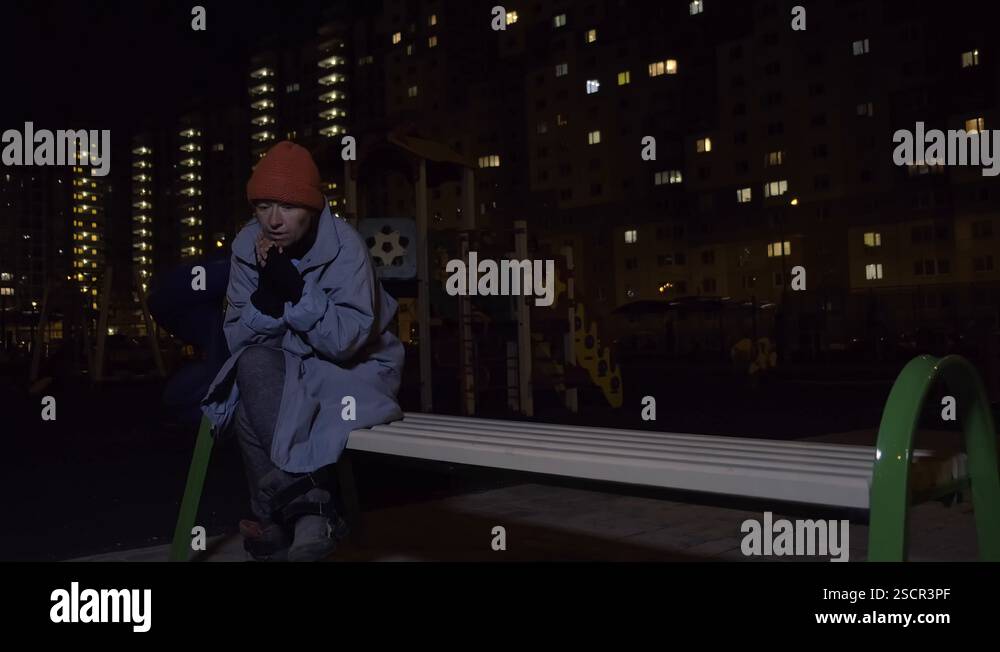 homeless person sits on bench in playground against background of night ...