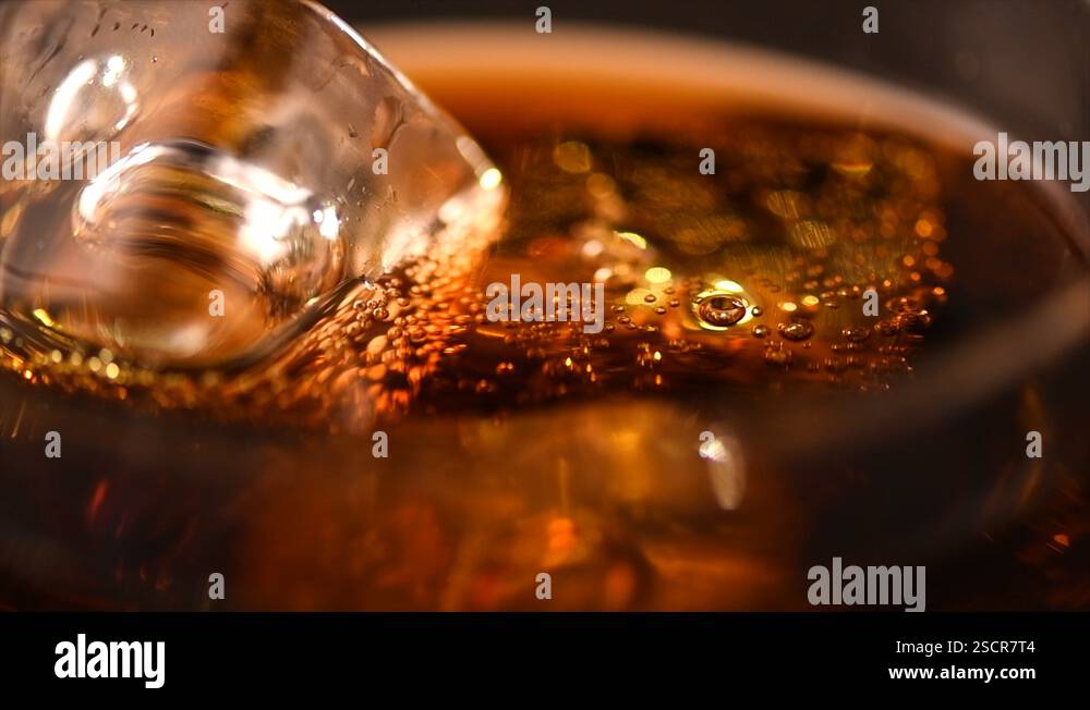 Coke with ice cubes closeup. Glass of fizzy cola rotated over brown ...