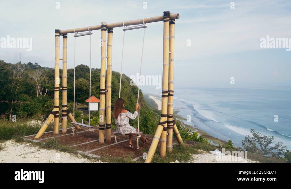 Backside view of young woman swings on swing with beautiful view on ...