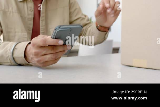 Holding smartphone, man checking package delivery status at home table ...
