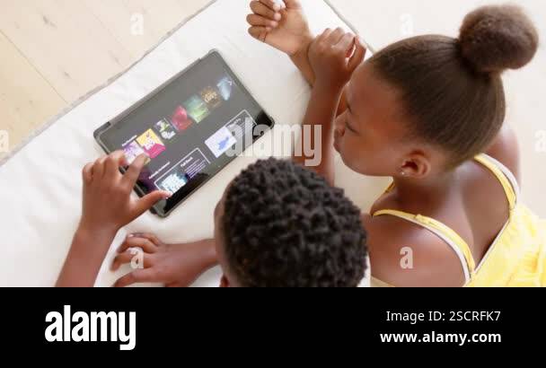 Using tablet together, African American brother and sister browsing educational content at home ...