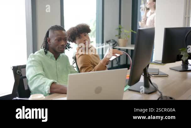 Collaborating on project, two colleagues using laptop and desktop in ...