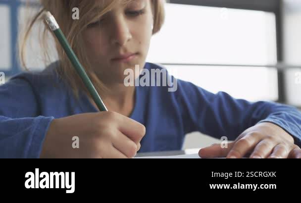 In school, child concentrating on writing with pencil in classroom ...