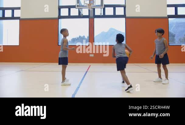 Playing basketball in school gym, three boys practicing dribbling and ...