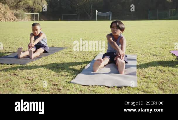 Stretching on yoga mats, children exercising outdoors during school PE ...