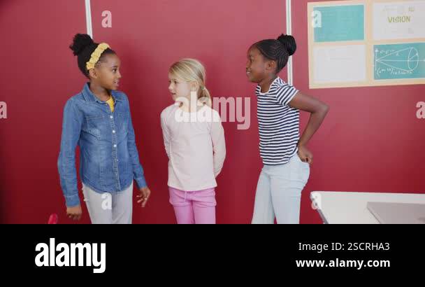 Talking together, three girls standing in school classroom, engaging in ...