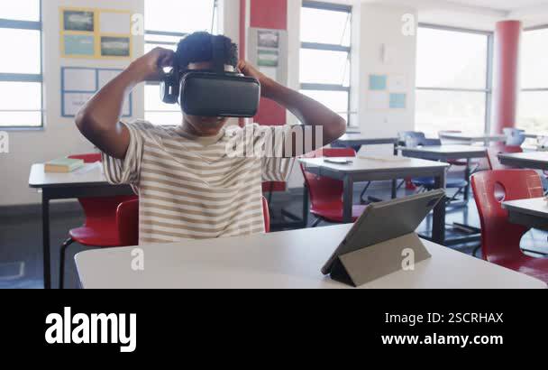 Using VR headset, boy interacting with tablet in school classroom. Technology, education ...