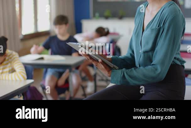In school, teacher using tablet while students studying in classroom ...