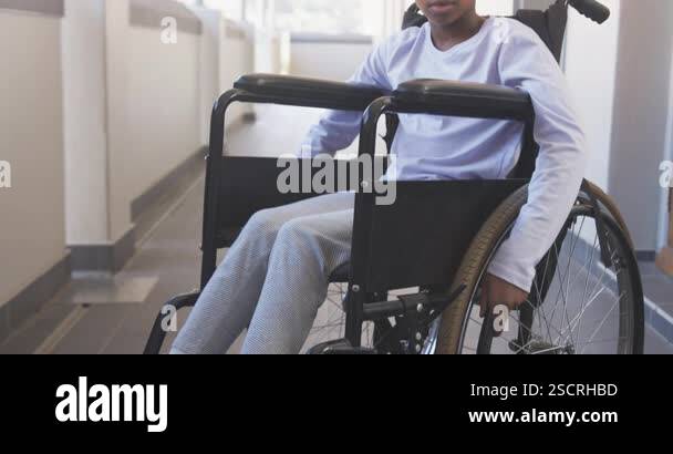 Smiling African American girl in wheelchair in school hallway, enjoying ...