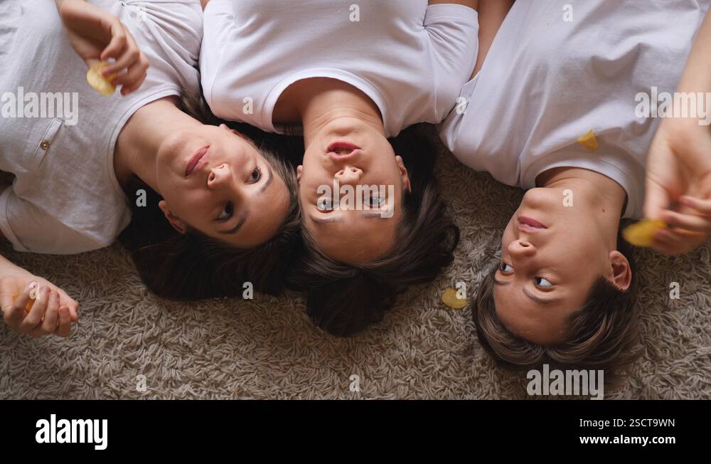 Funny eating snacks potato chips teenager triplet sisters girls lie on ...