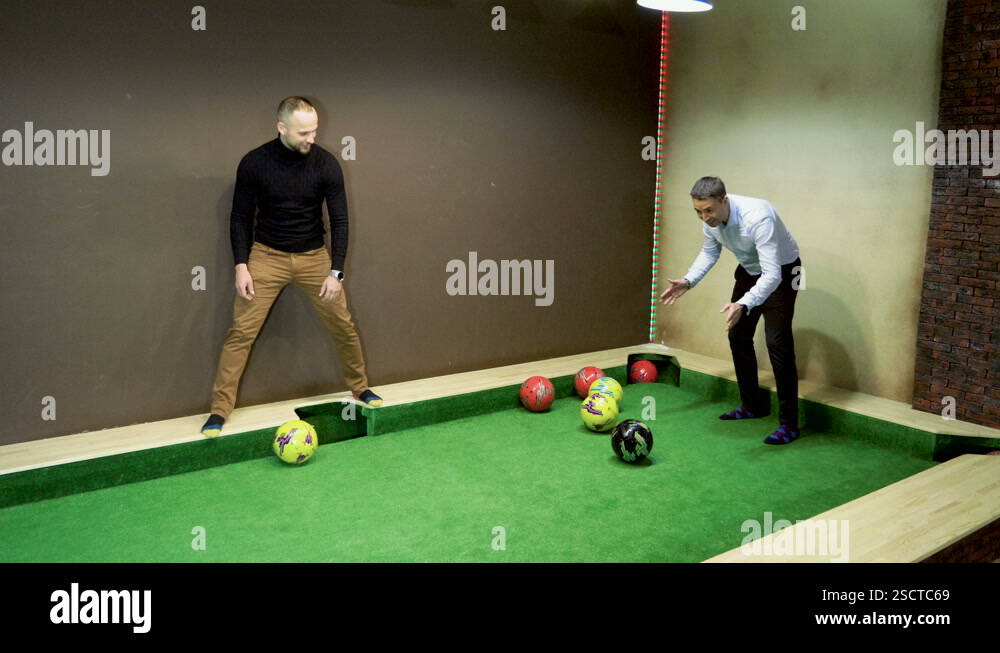 Two men playing billiards, hitting balls into holes on a floor billiard ...