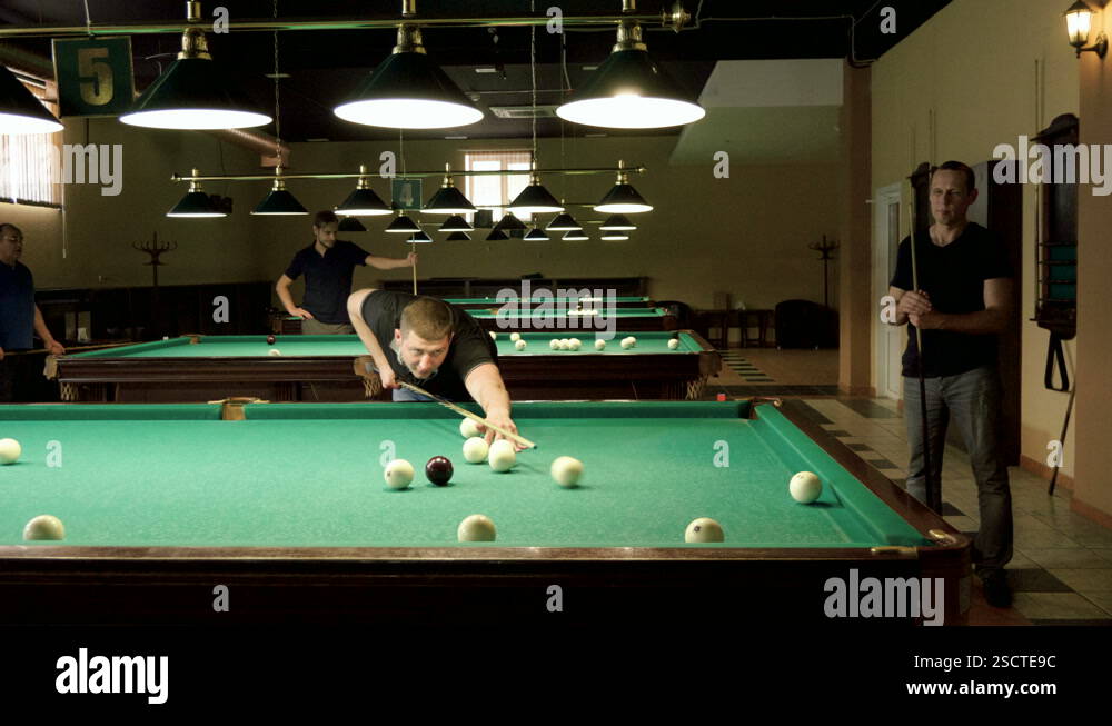 Men playing billiards, hitting balls with cue into pockets on billiard ...
