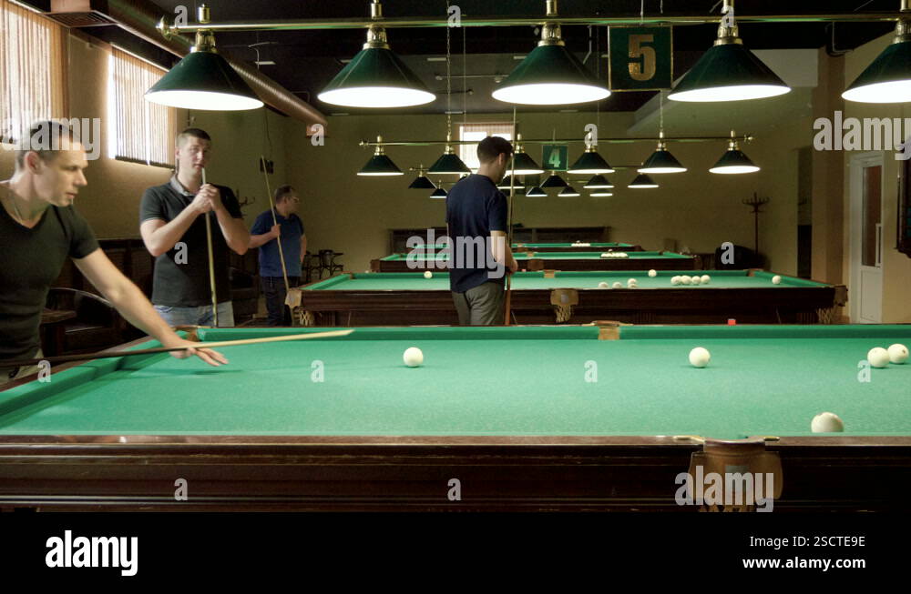 Men playing billiards, hitting balls with cue into pockets on billiard ...