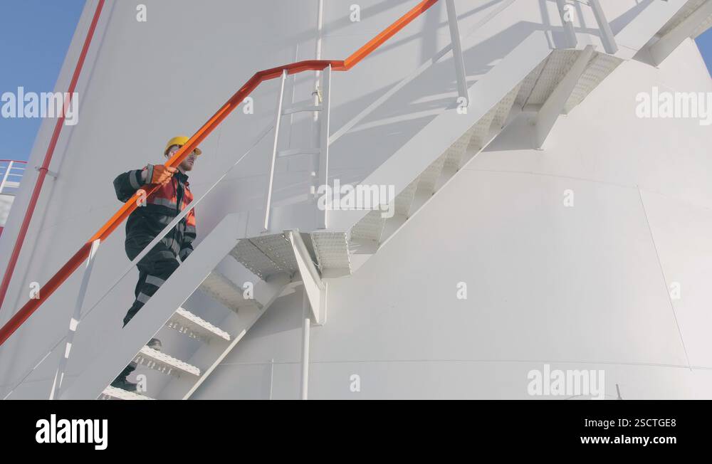Petrochemical engineer climbs staircase of fuel tank, stops and wipes ...