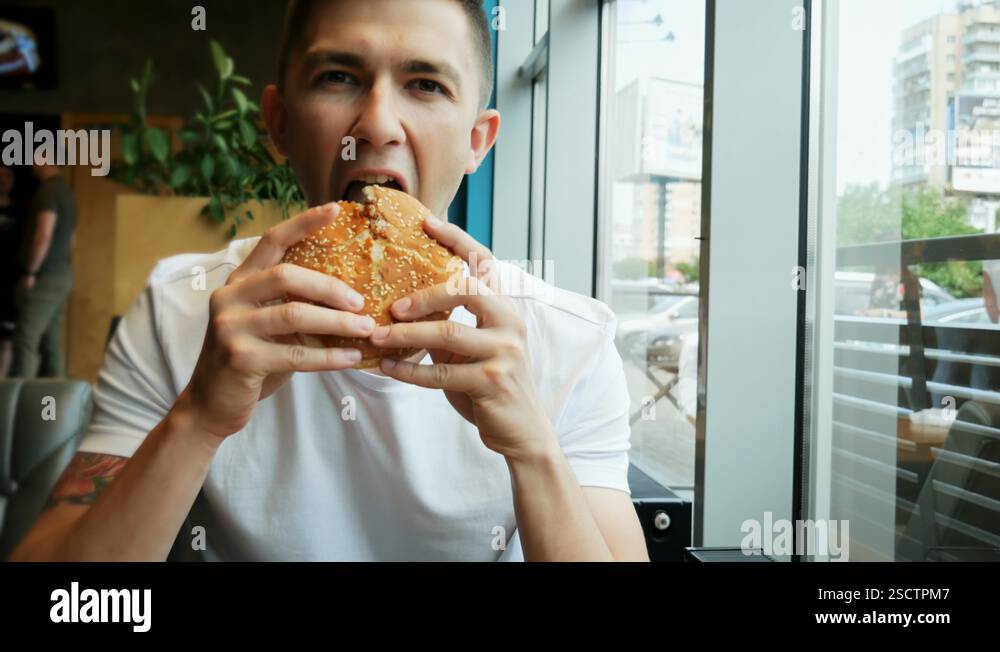 Young handsome guy eats hamburger in a diner, fast food restaurant ...
