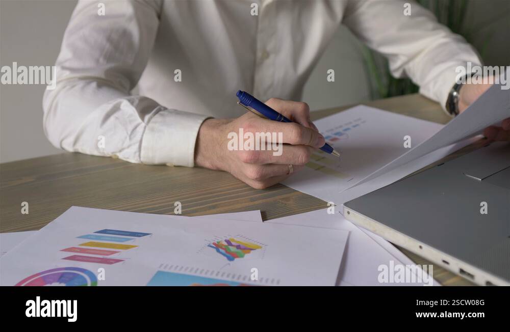 close-up businessman takes notes in documents, graphs and works behind ...