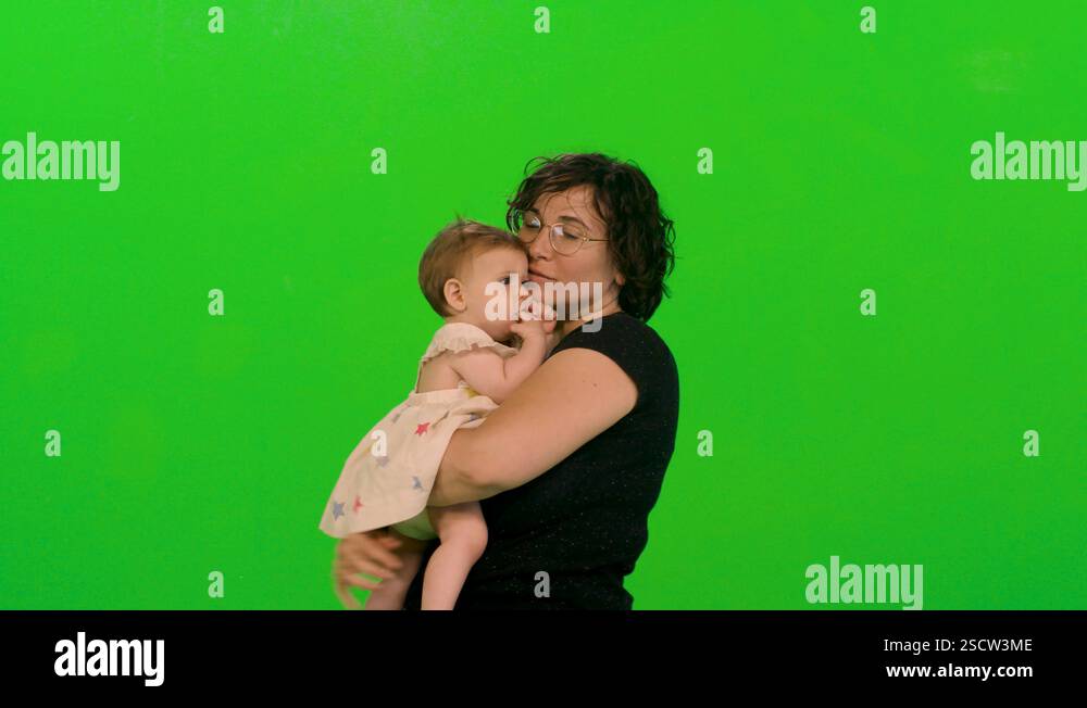 Young mother holds and hug her sleepy baby girl over a green screen ...