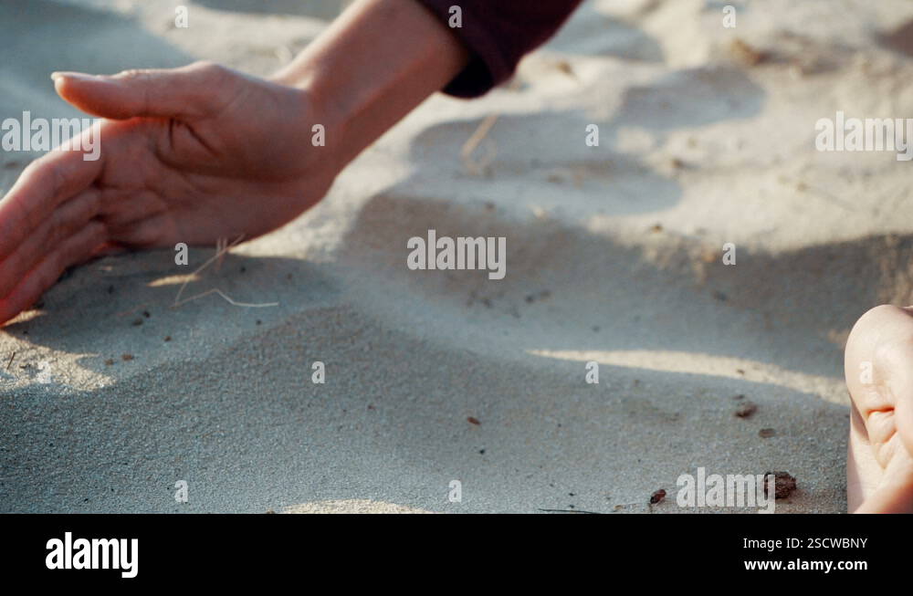 SLOW MOTION, CLOSE UP: The sand passes through the fingers of a young ...