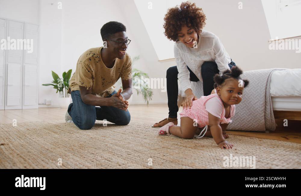 Baby Girl Learning To Crawl At Home As Parents Sit On Floor And Give ...