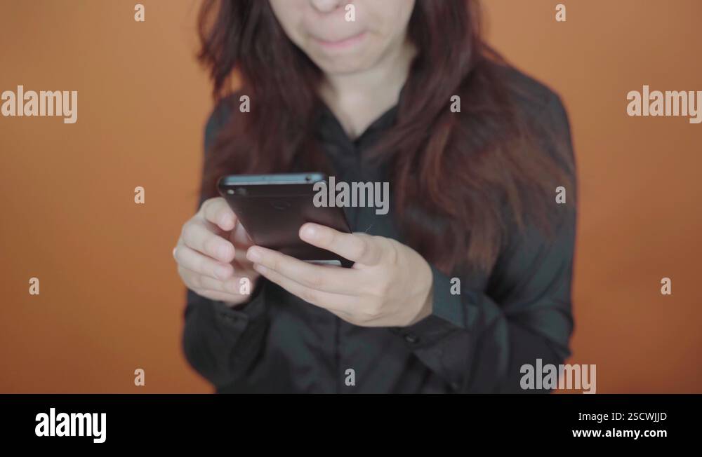 Young woman holding mobile phone in hand on orange background. Female ...