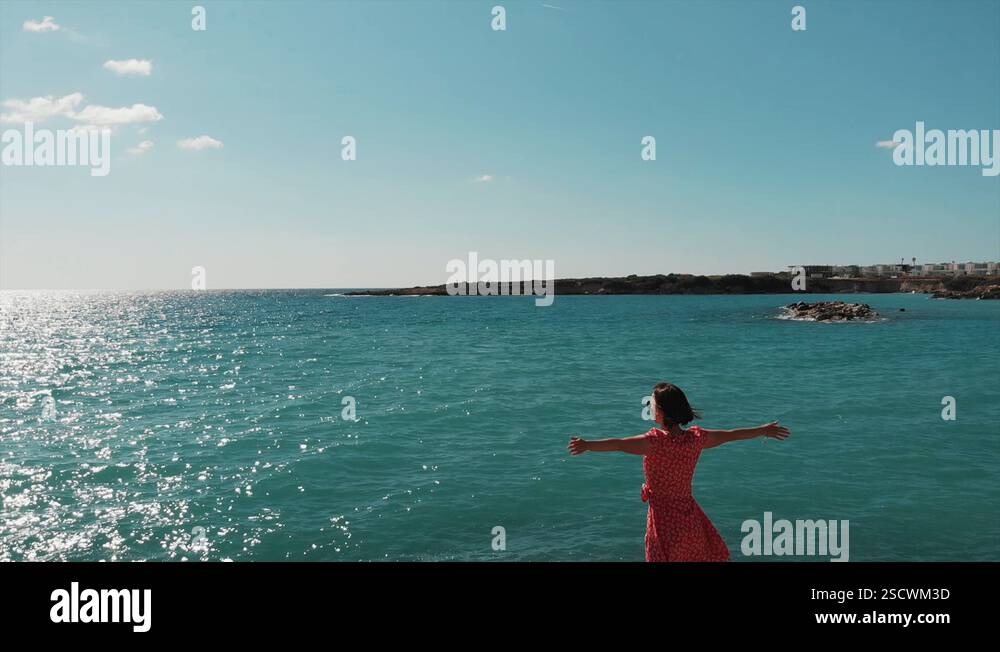 Cute fit woman in red dress with hands apart standing on the cliff ...