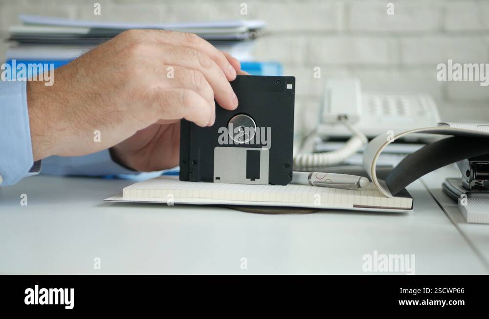 Man in the Office Sitting on the Desk with a Floppy Disk in His Hand ...