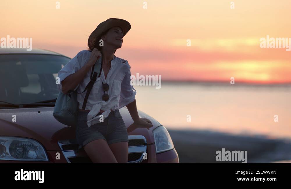 Pleasant young travel woman relaxing waving hair sitting on car bonnet ...