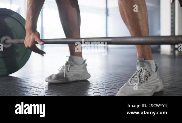 Lifting barbell, man wearing smartwatch and athletic shoes in gym ...