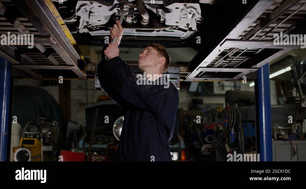 4K Young mechanic working underneath a vehicle & smiling at camera ...