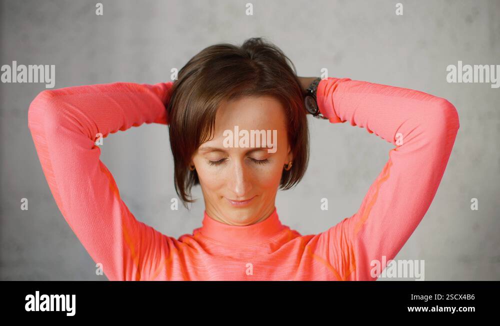 Woman puts hands on back of head and tilts head forward stretching neck ...