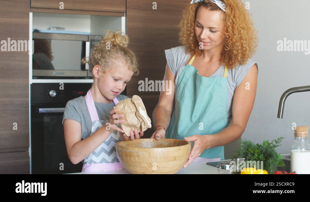 Little girl and her mother sprinkling flour into a bowl and smiling ...