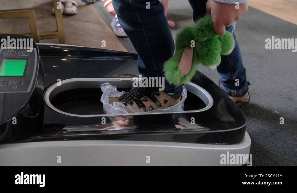 Little boy putting on foot in automatic shoe cover dispenser Stock ...