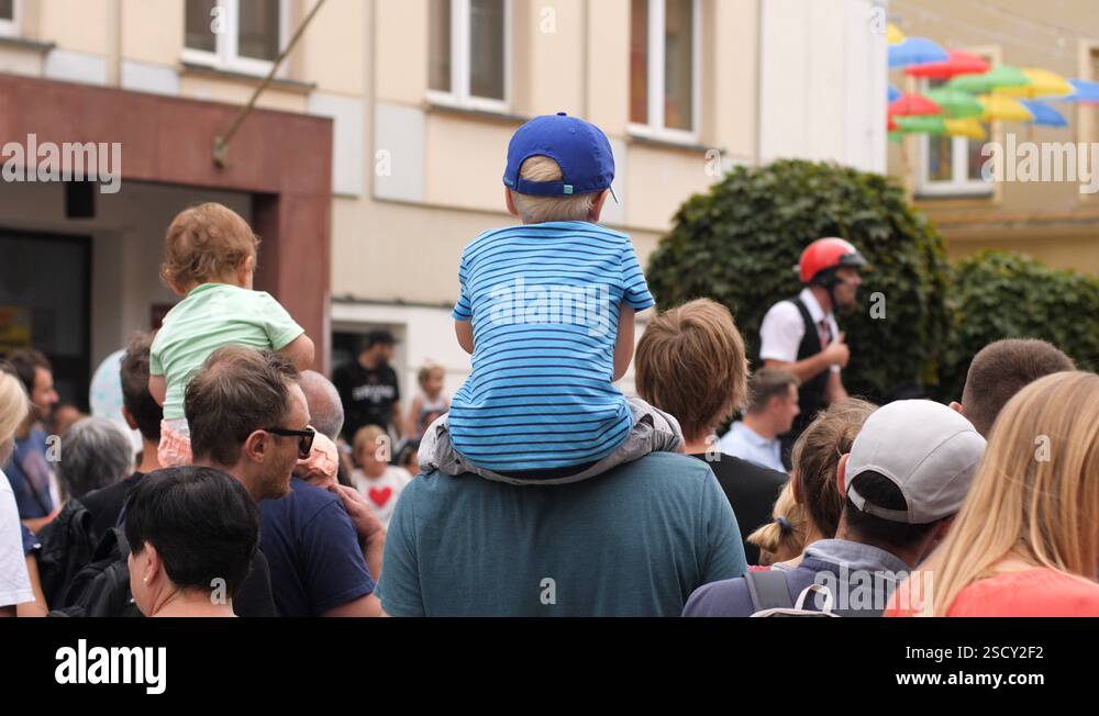 Parent father stay in crowd people holds a child sitting on shoulders ...