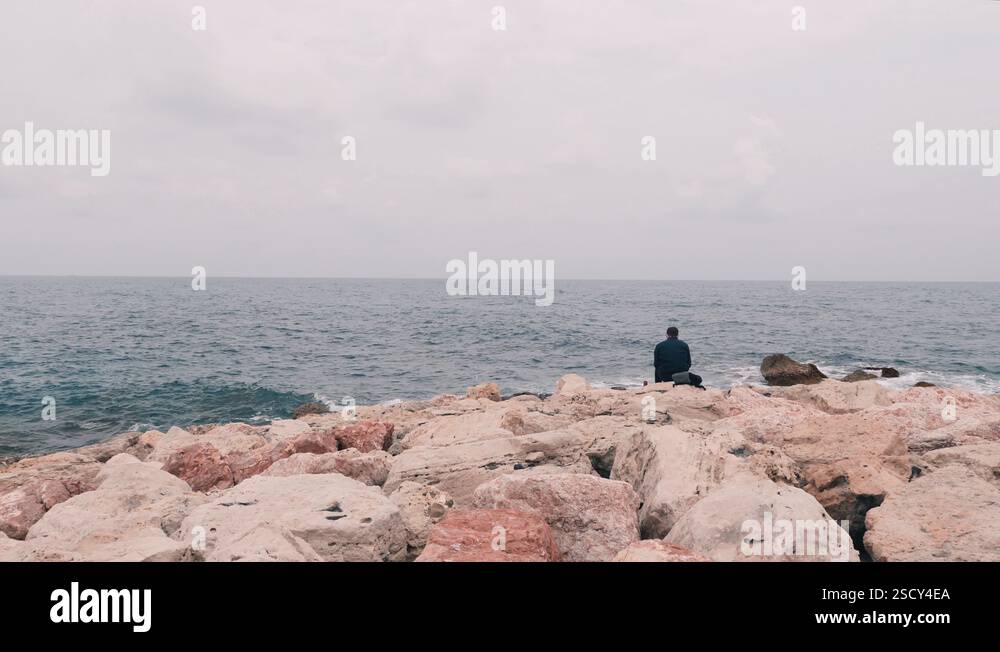 Lonely sad man sitting on big stone near ocean. Office worker sitting near sea Stock Video ...