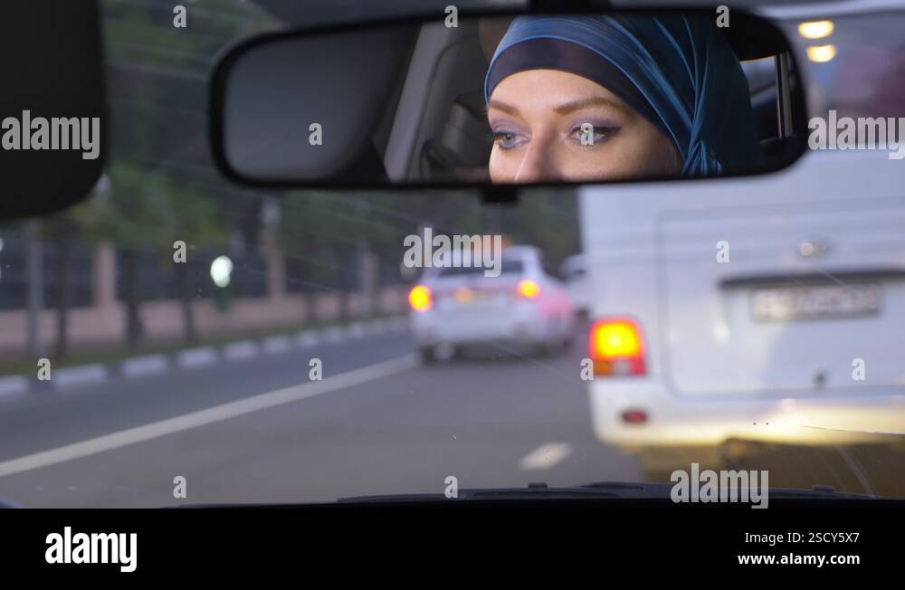 reflection of a woman in a hijab in a rearview mirror of a car while ...