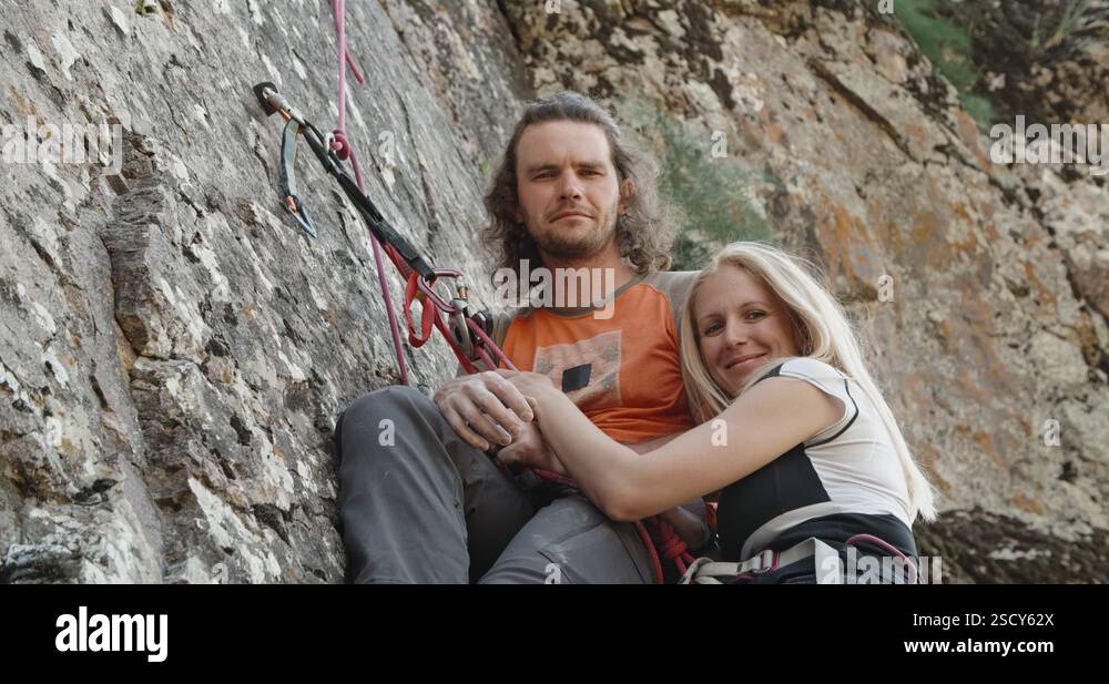 Male and female alpinists are climbing a steep cliff together, looking ...