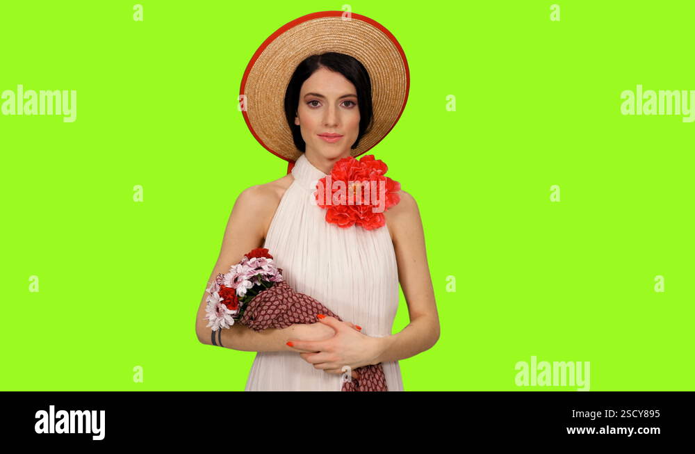 Charming girl in straw hat stands with bunch flowers waving hi on green ...