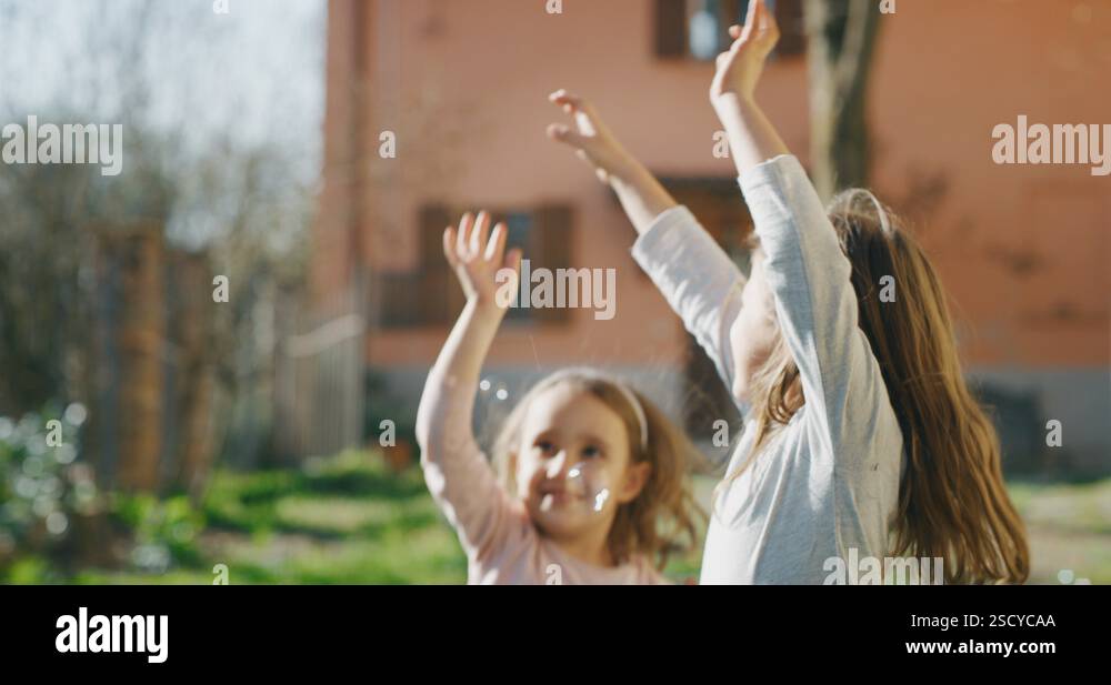 Two little girls are having fun playing with soap bubbles outside their ...